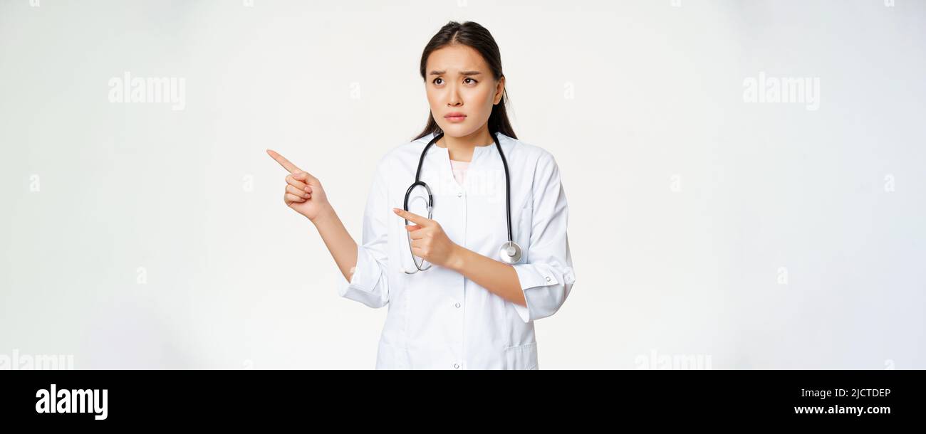 Skeptical female doctor, concerned nurse pointing and looking left with ...