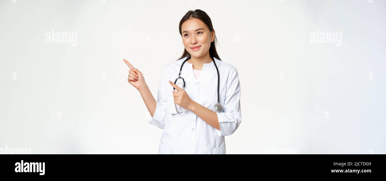 Pleasant smiling female doctor in uniform, pointing fingers and looking ...