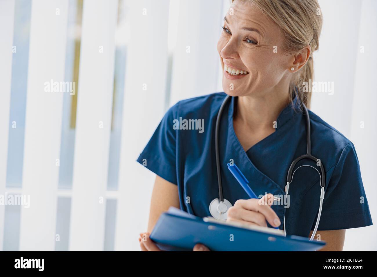 Smiling woman doctor taking notes on clipboard and looking on patient ...