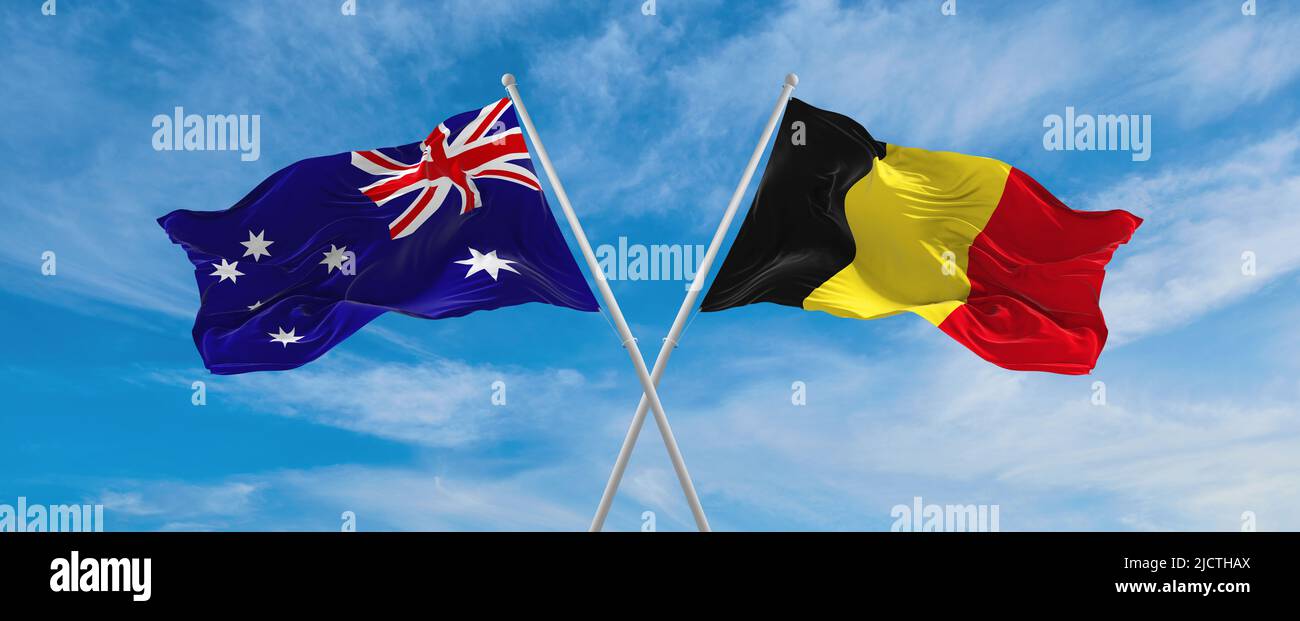 two crossed flags Australia and Belgium waving in wind at cloudy sky ...