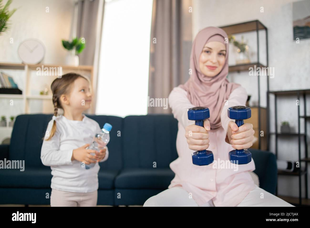 Focus on dumbbells, young Arab family doing sports in a bright living ...