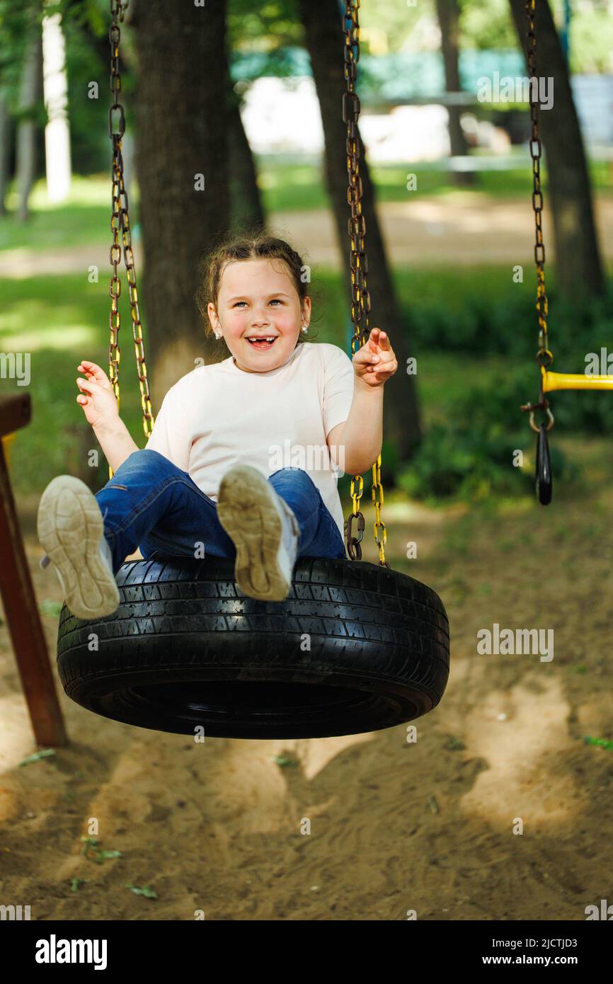 Happy little girl swinging on car rubber wheel in playground in green ...