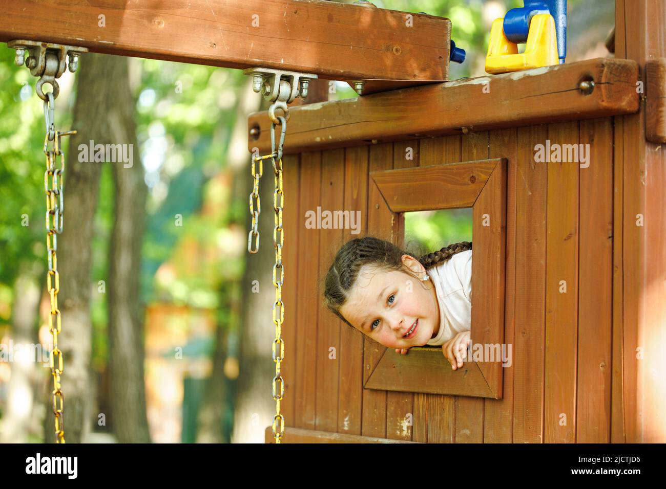 Cute little girl leaning head out window in playground in children ...