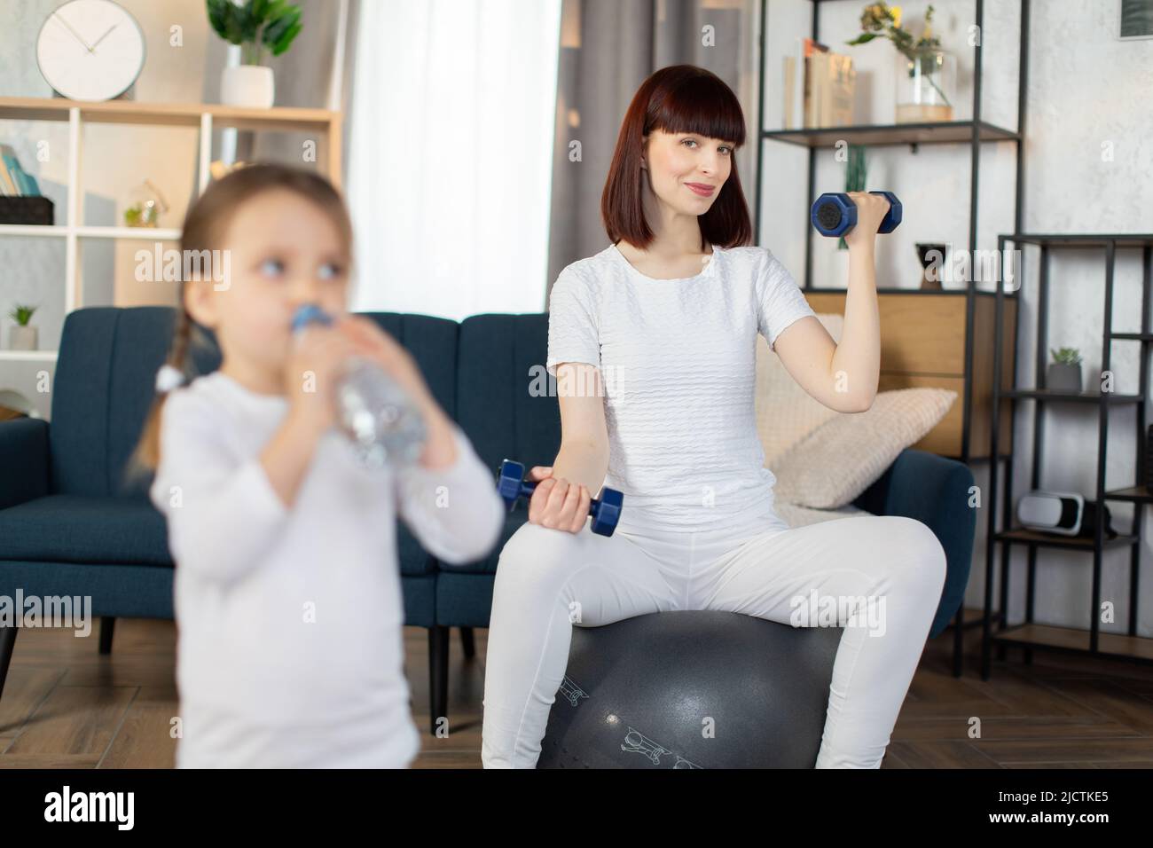Young sporty mom sitting on a fitness ball and doing sports exercises ...