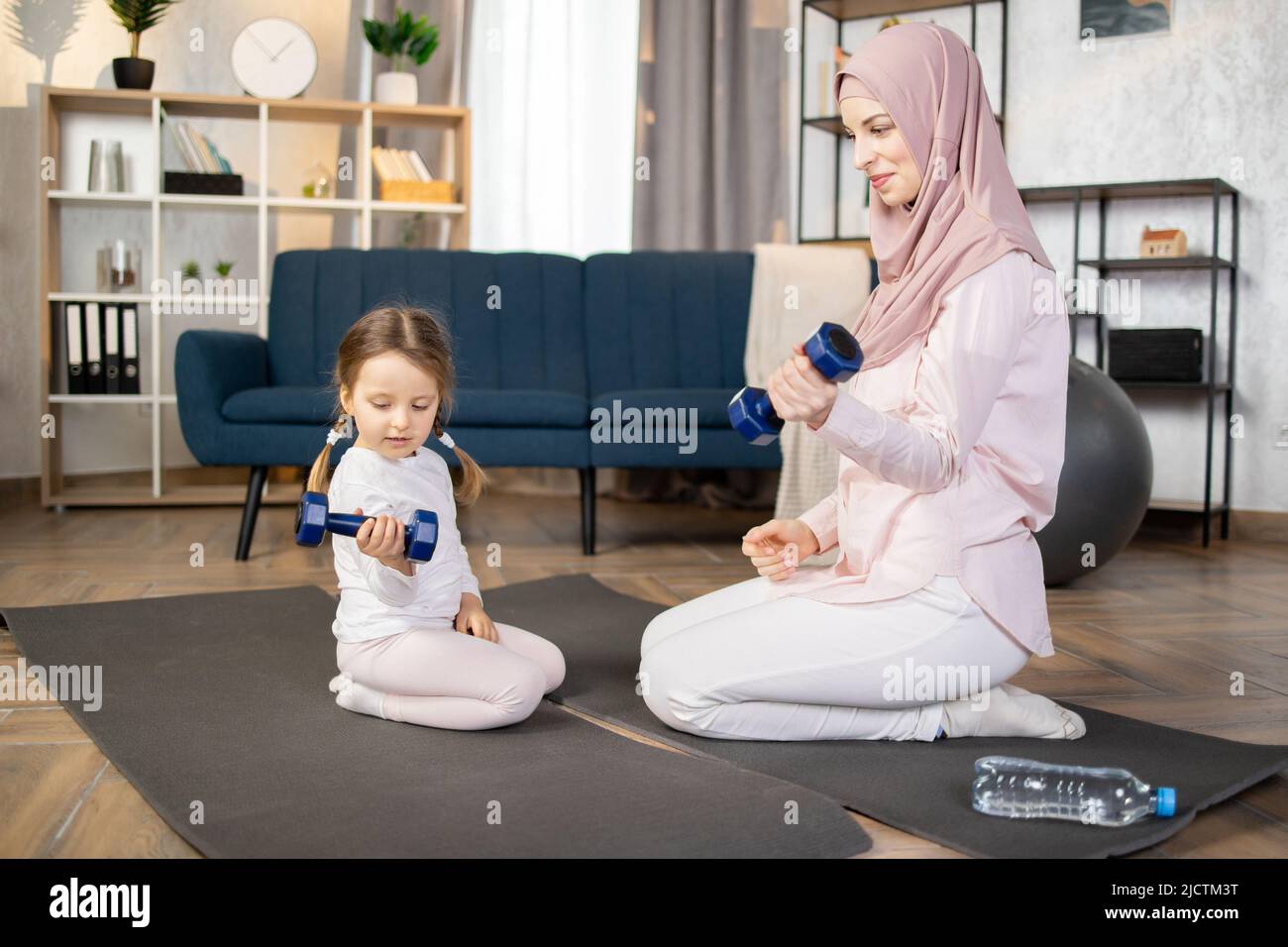 Cute little girl doing sports with her Muslim mother in a hijab sitting ...