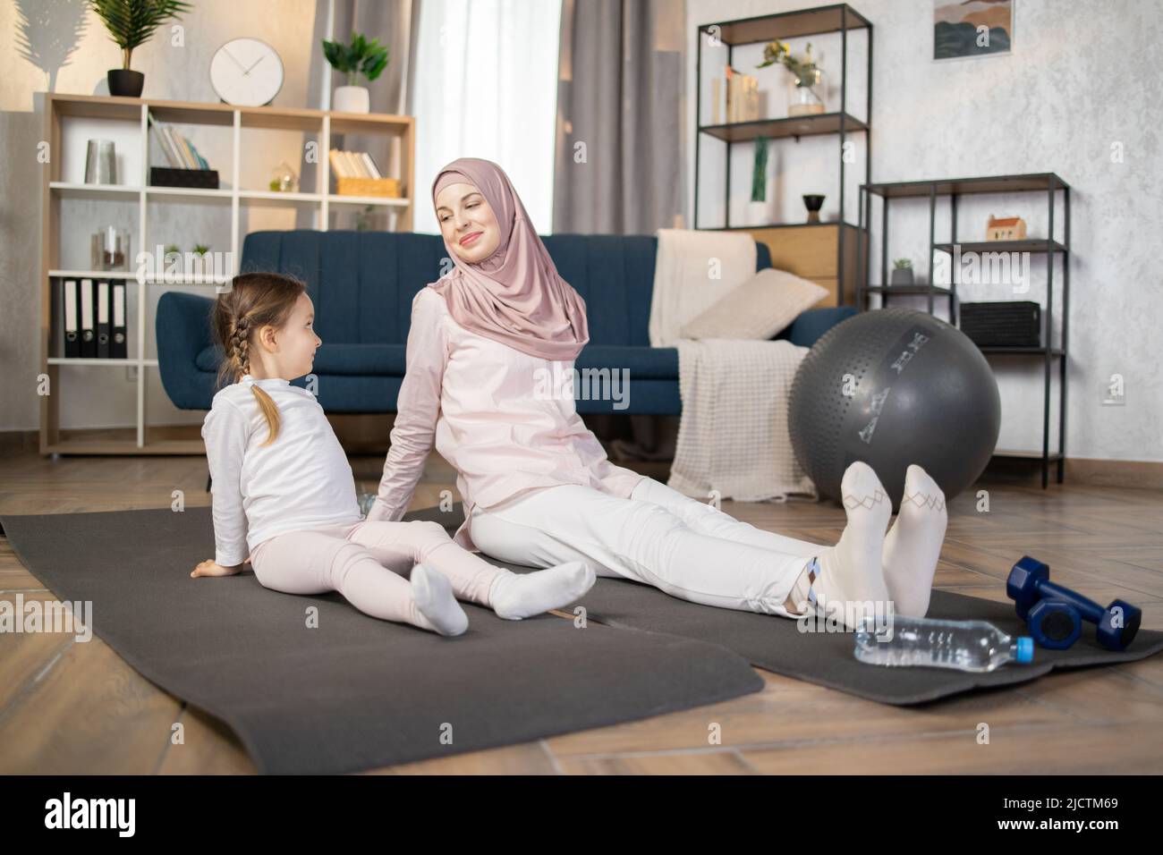 Young smiling muslim mother doing sports exercise at home, wearing ...