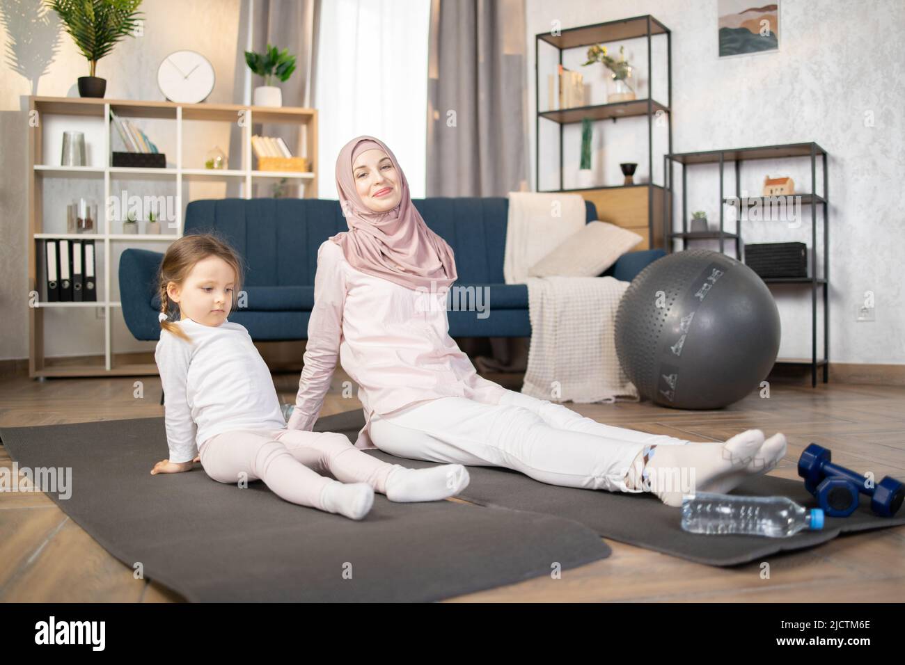 Young smiling muslim mother doing sports exercise at home, wearing ...