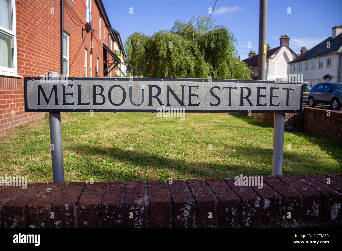 Melbourne Street name sign on two posts with grass and buildings in the ...