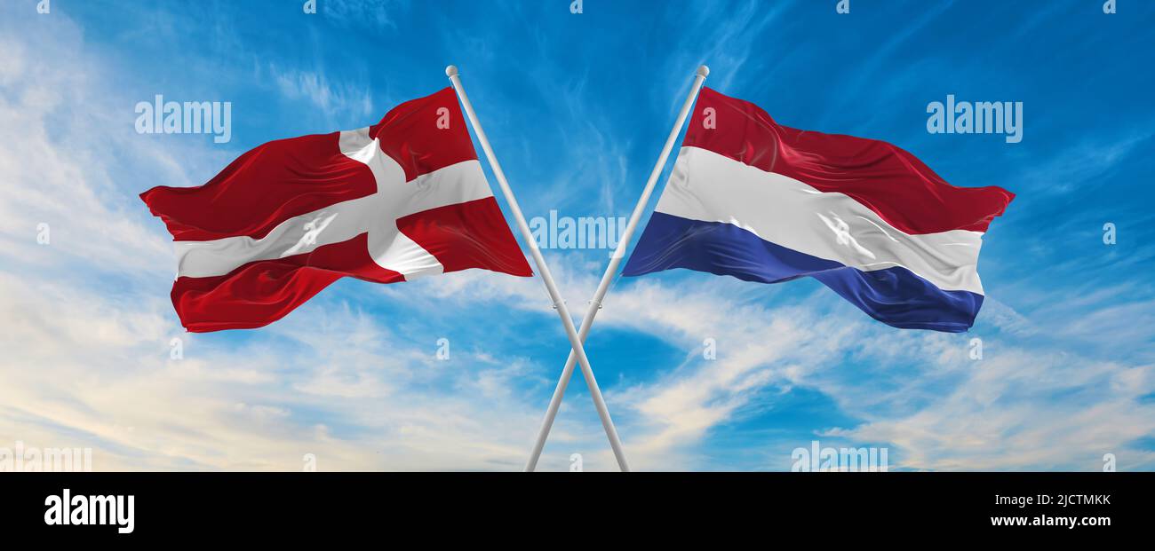 two crossed flags denmark and Netherland waving in wind at cloudy sky ...