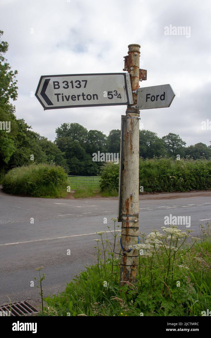 white road sign to Tiverton and Ford with a road and hedges in the ...