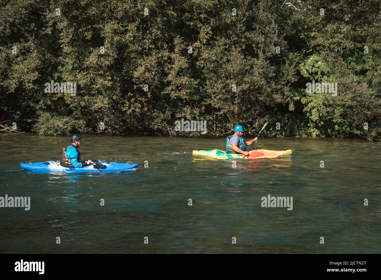 Two kayakers paddling and maneuvering on the fast-moving river with a ...