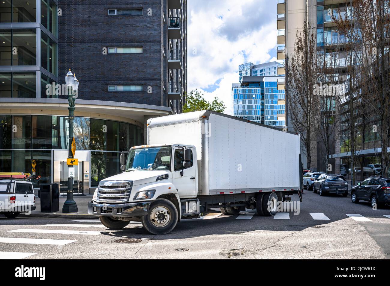Big rig day cab white semi truck with long box trailer making local ...