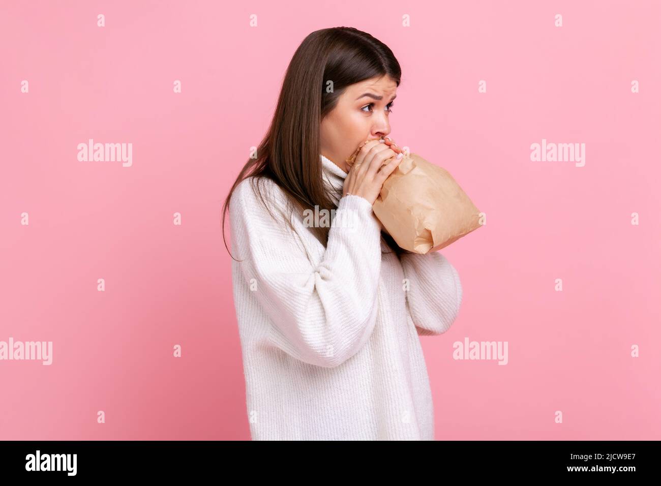 Side view of nervous girl breathing into paper bag to improve state of ...