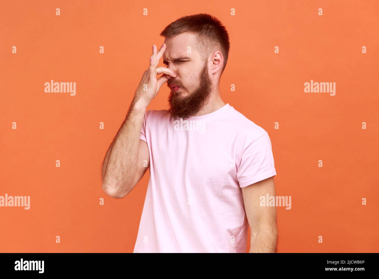 Portrait of confused bearded man grabbing nose, grimacing in disgust and expressing repulsion to ...