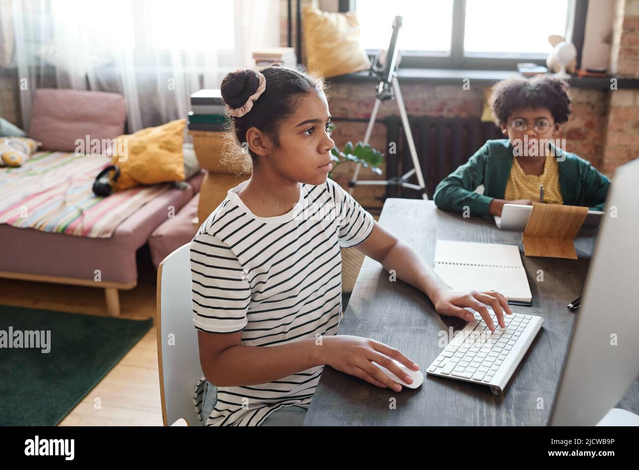 African girl using computer while sitting at table together with her ...