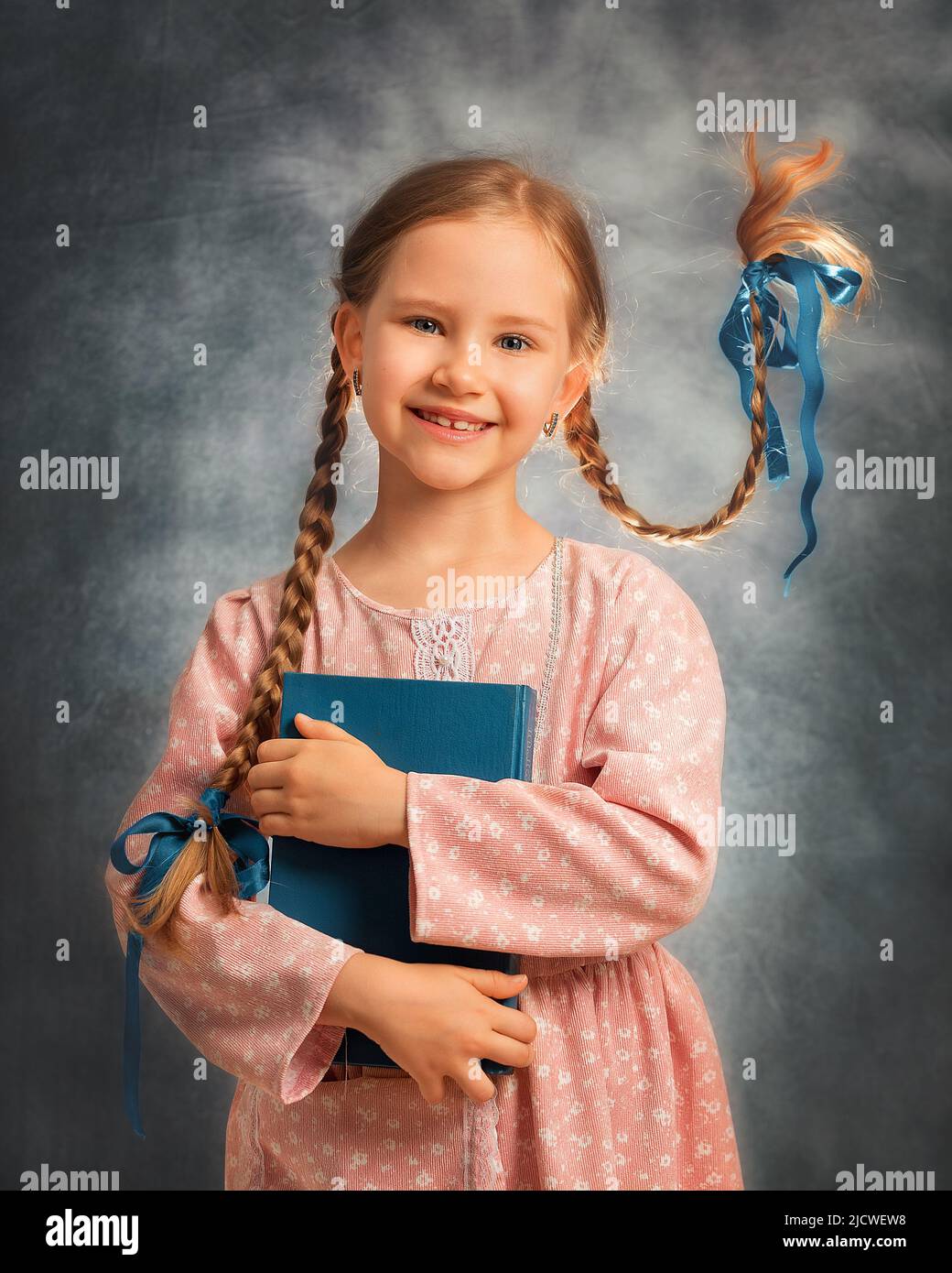 Close portrait of a happy girl kid with two flying braids on a gray ...