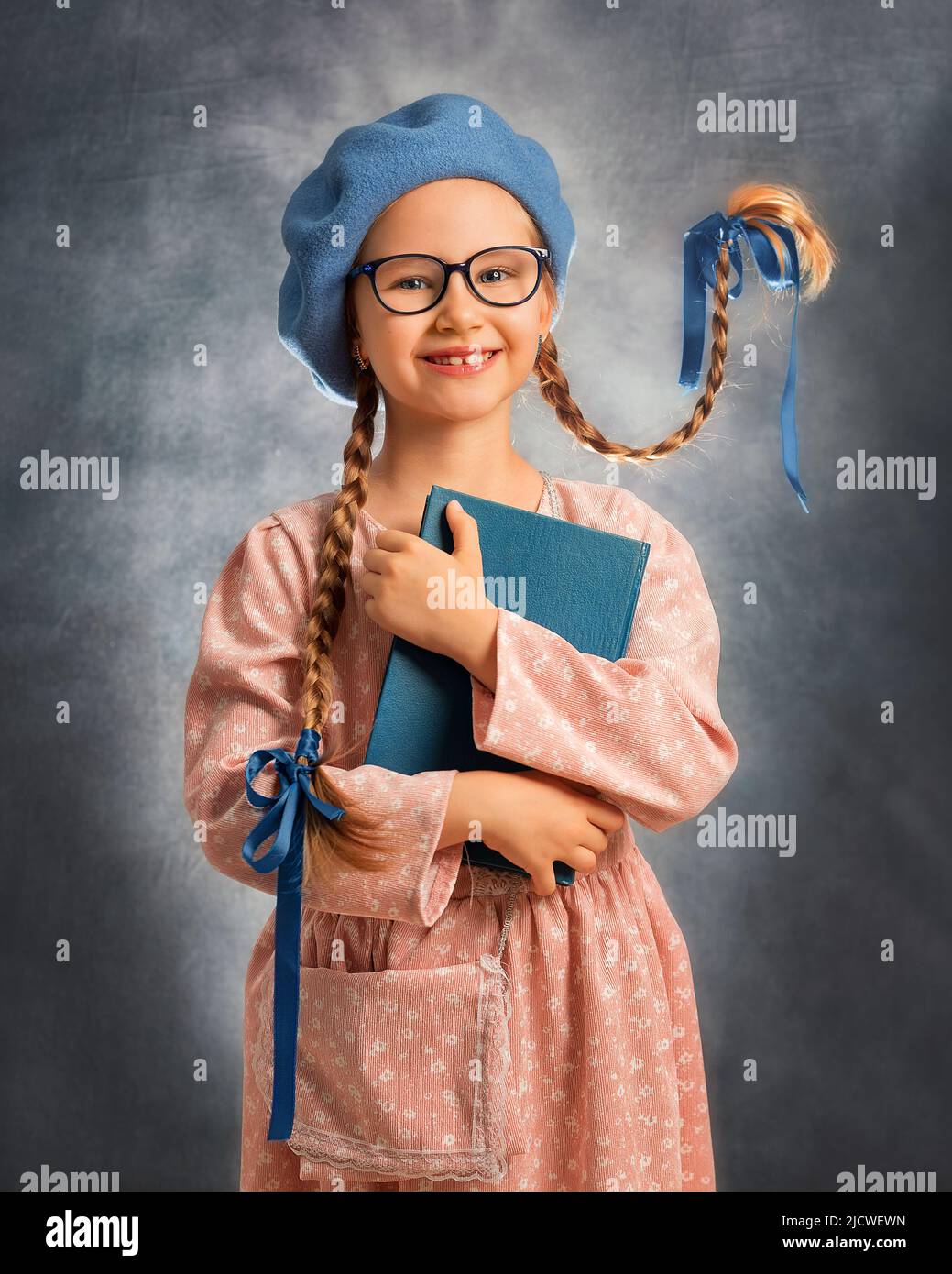Close portrait of a happy girl kid with two flying braids on a gray ...