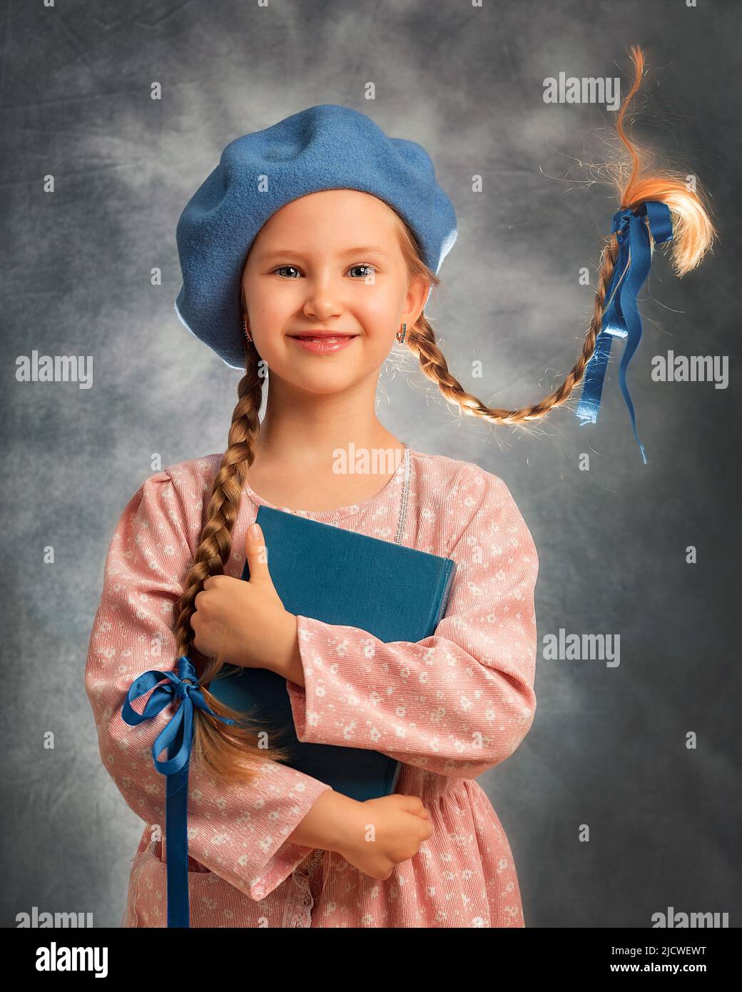 Close portrait of a happy girl kid with two flying braids on a gray ...