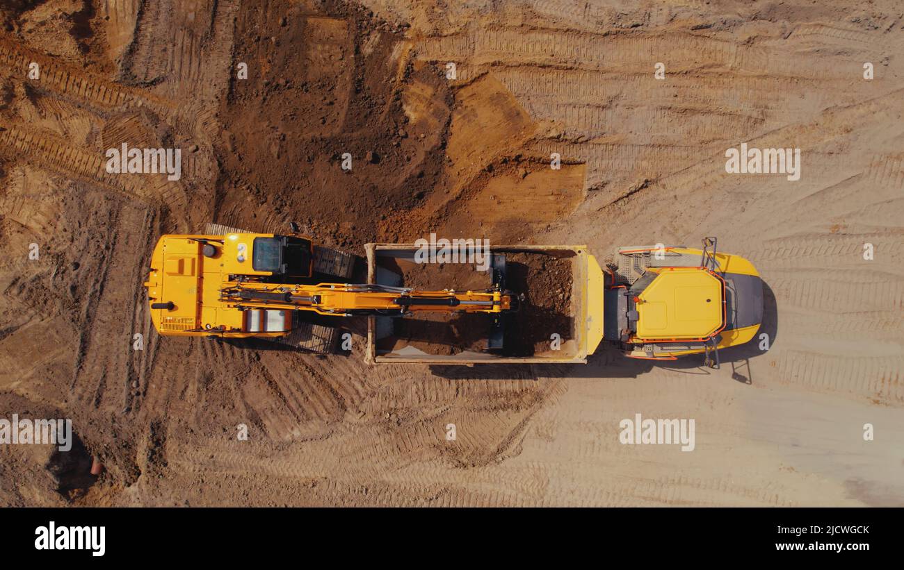 Aerial view of a yellow digger and a tipper truck. Digger loading piles ...