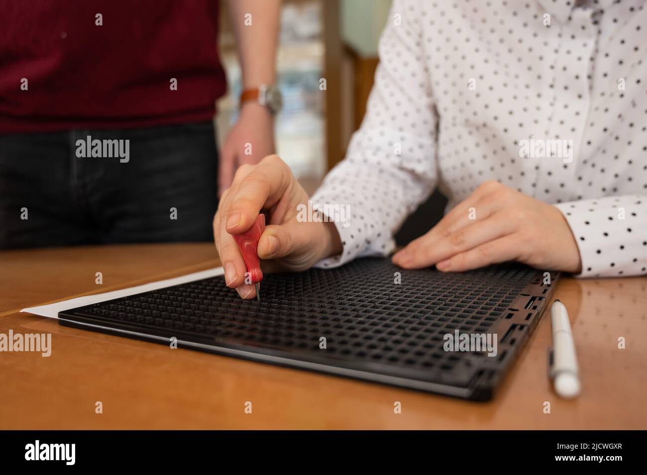 A man teaches a woman how to use a special stencil and stylus to write ...
