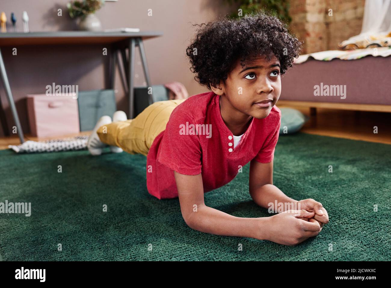 African little boy standing in the bar on floor and watching TV during ...