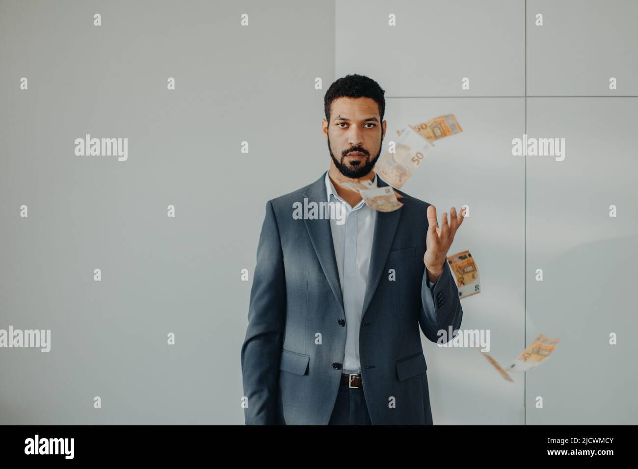 Serious young businessman man standing in officethrowing money away ...