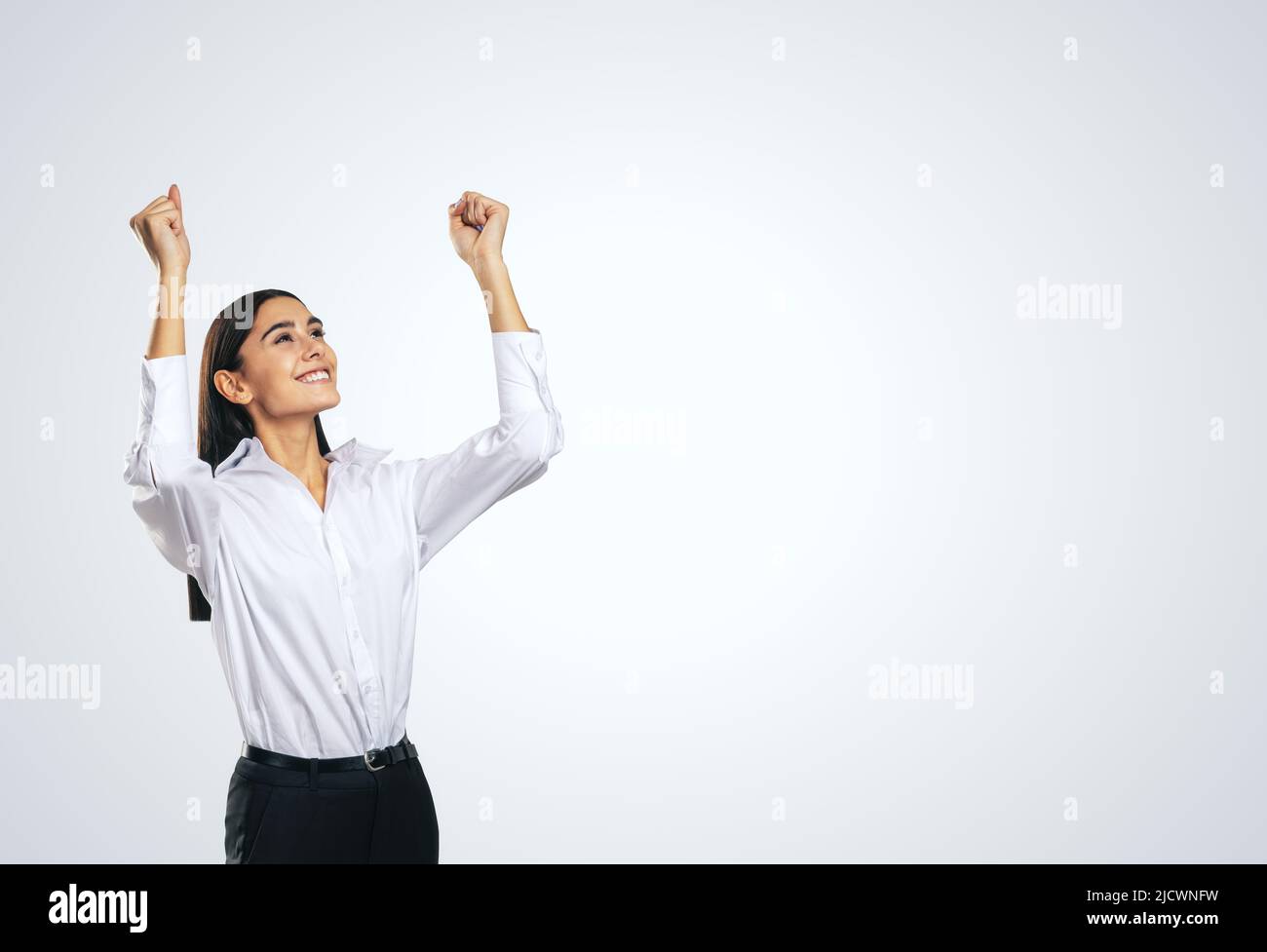 Joyful and satisfied woman in white shirt with raised hands showing her ...