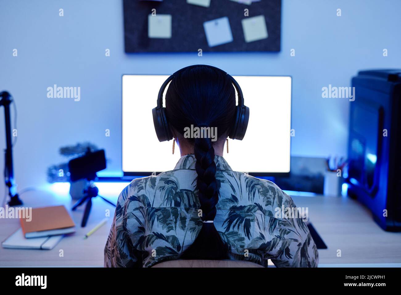Back view of teenage girl playing video games at night with blue neon ...