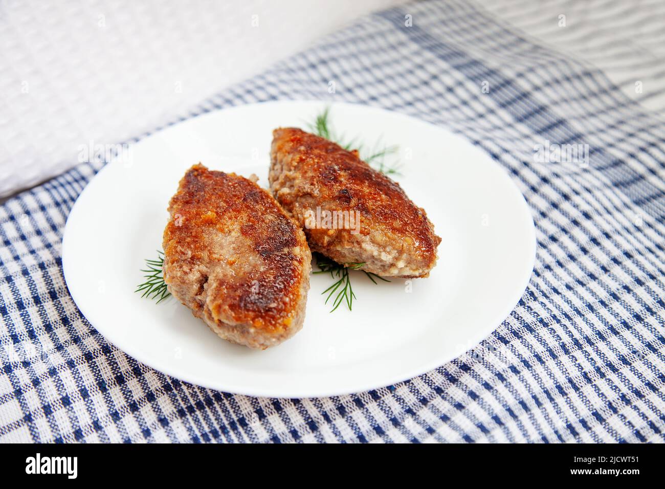 White plate with beef cutlets laying on traditional cheched kitchen ...
