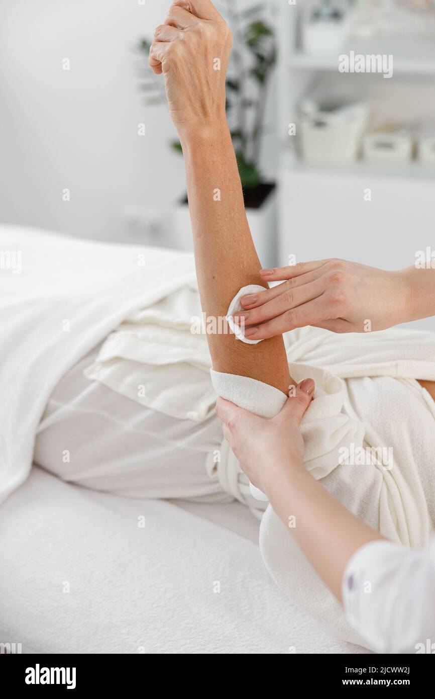 Vertical shot of dermatologist hands cleaning female arm skin applying ...