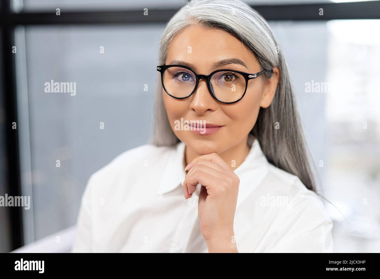 Portrait of senior gray-haired female doctor sitting at the desk in the ...
