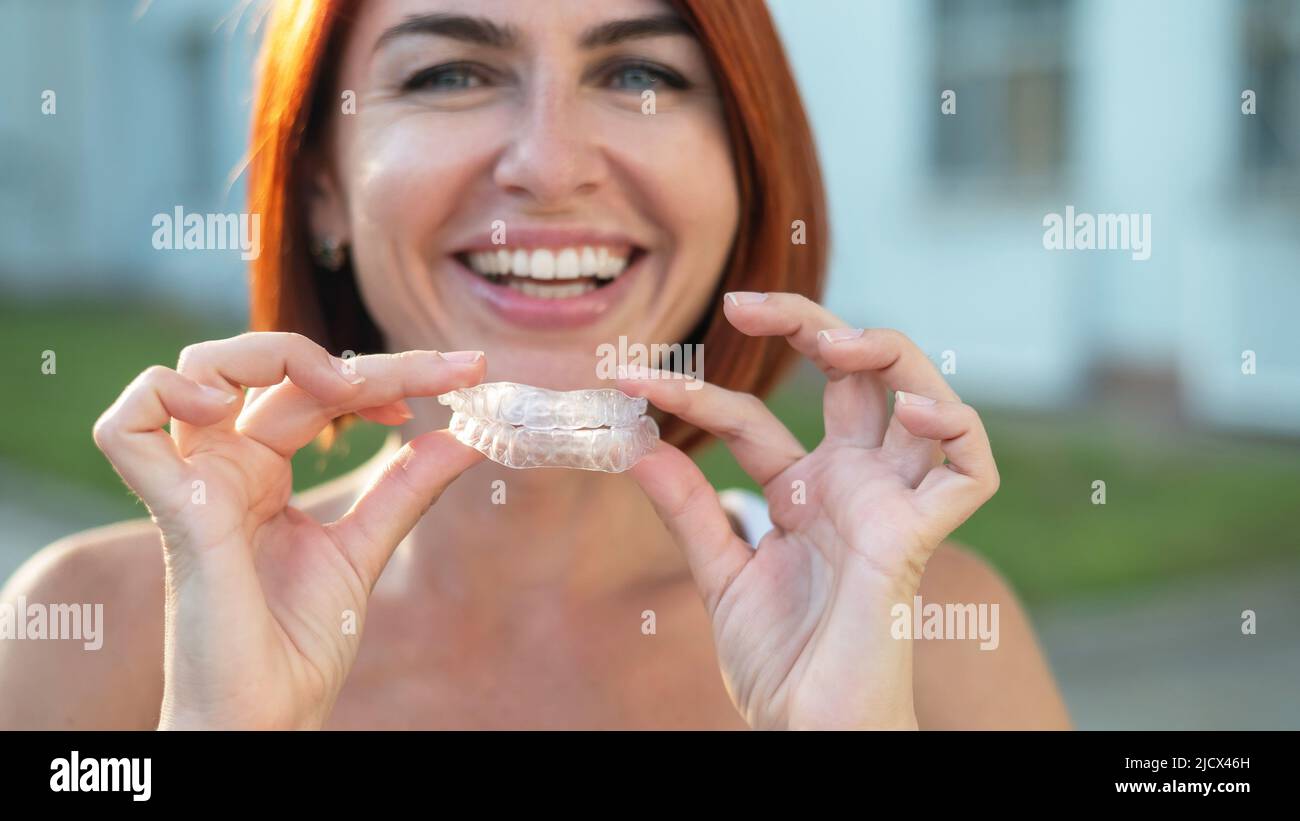 Red-haired Caucasian woman holding transparent mouthguards for bite ...