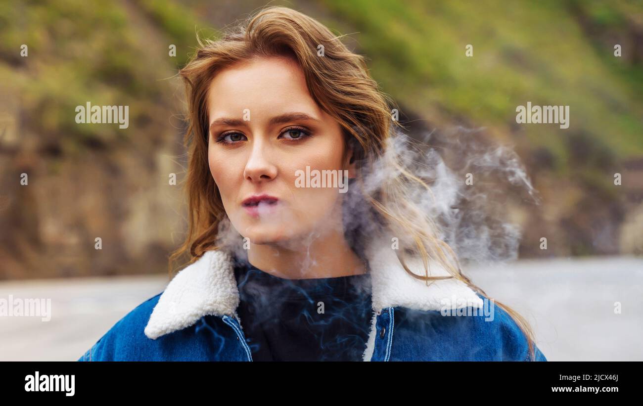 young woman in a denim jacket smokes a cigarette near the road Stock ...