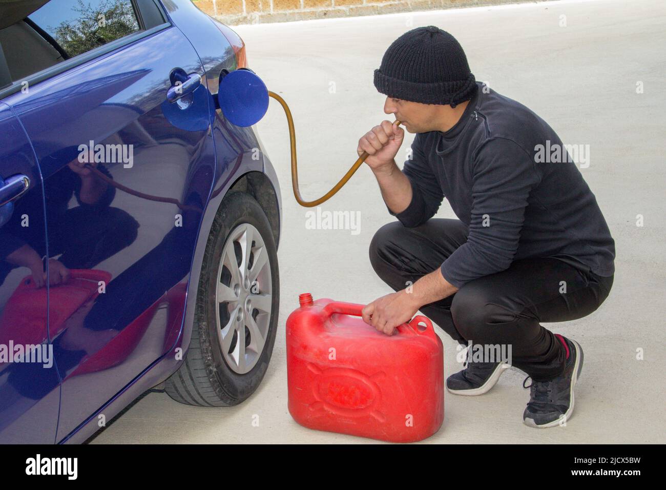 Image of a thief dressed all in black sucking gasoline from a parked ...