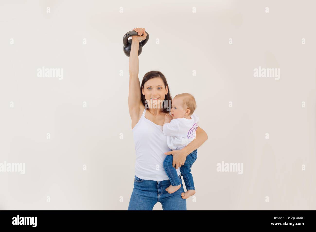 Young athletic smiling woman lifting up kettlebell and holding little ...