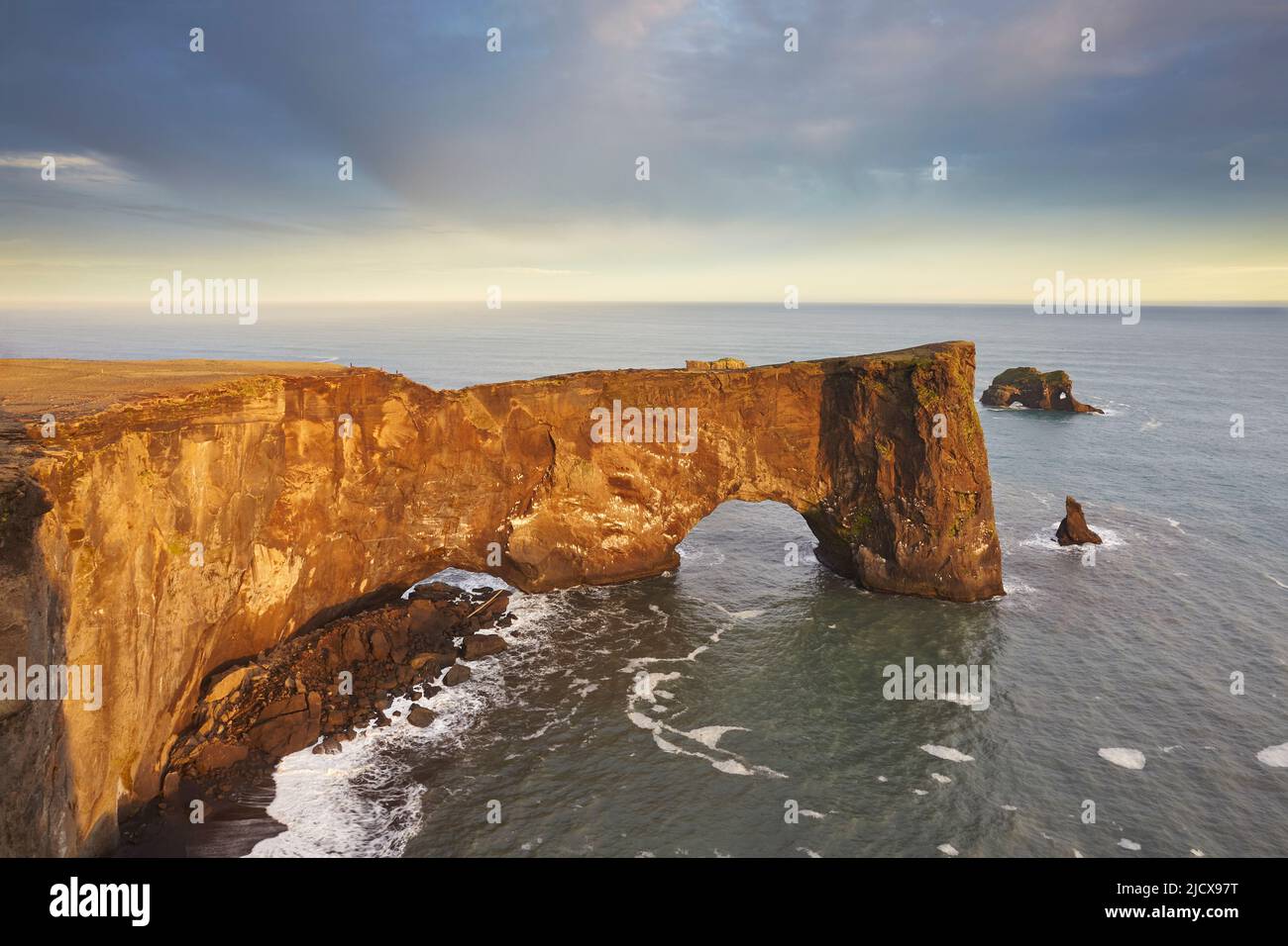 A rock arch on Dyrholaey Island seen in sunset sunlight, near Vik ...