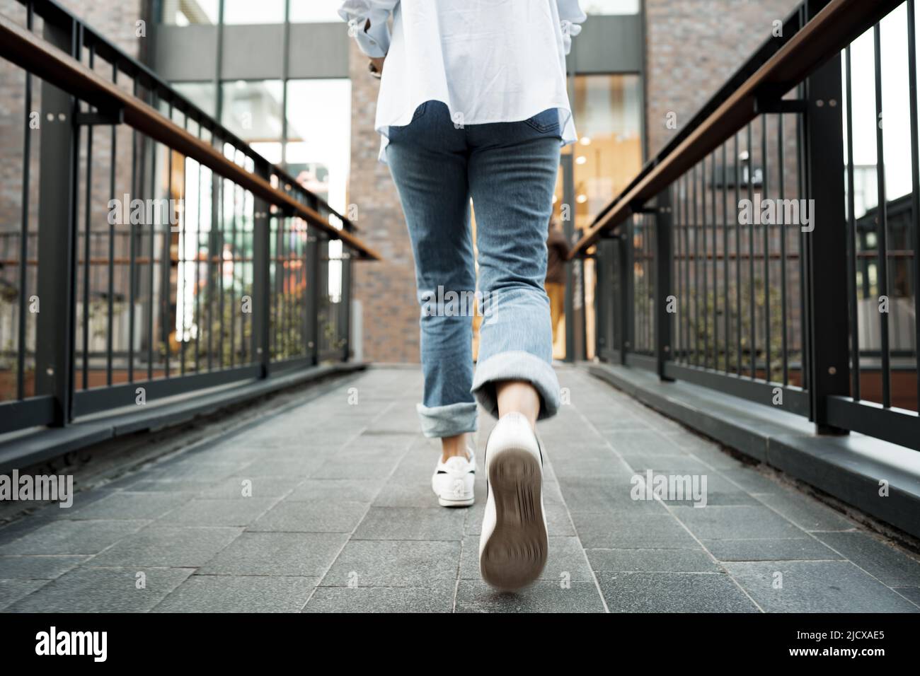 Back view of a woman in jeans and sneakers walking in the street Stock ...