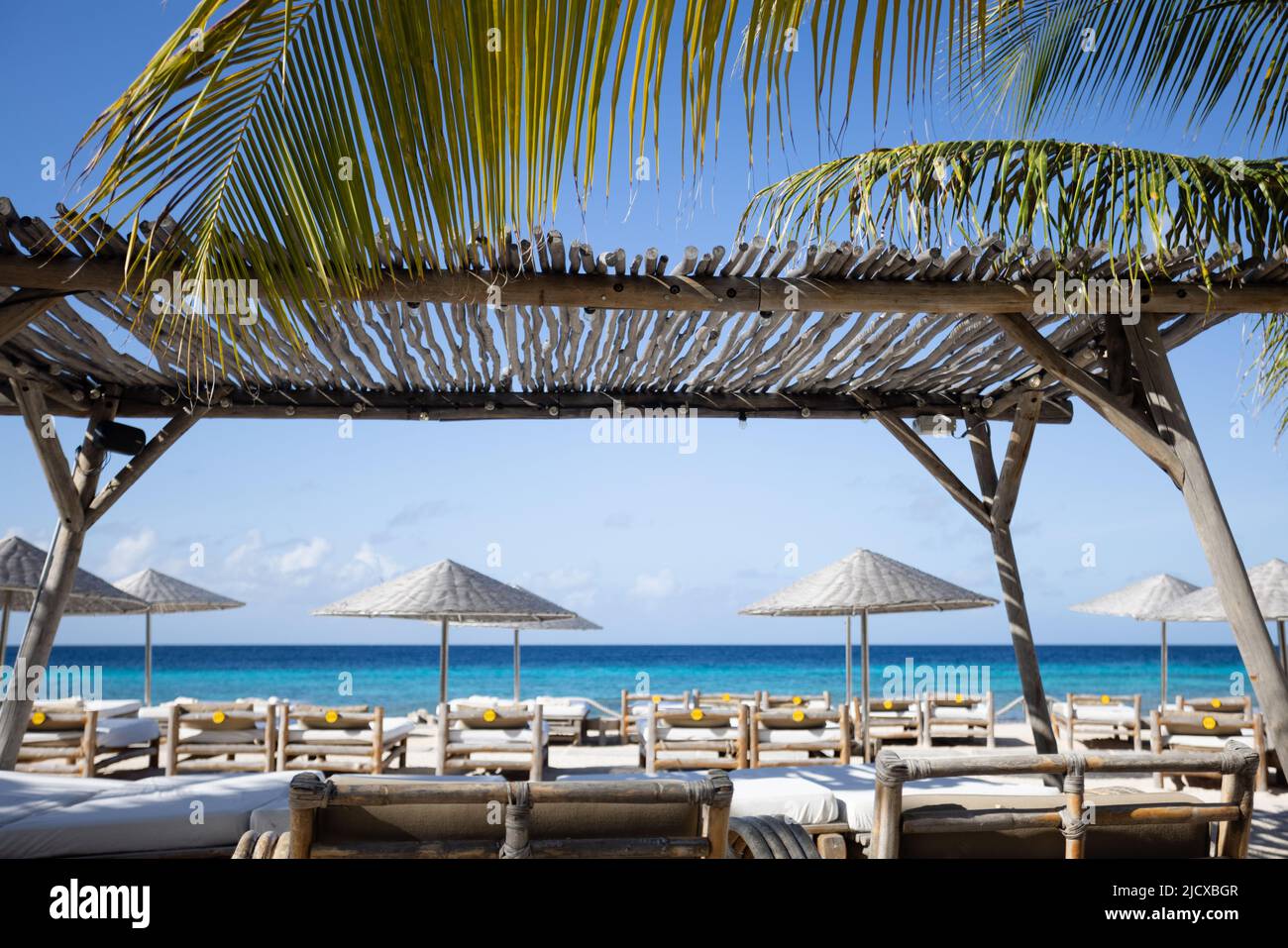 Wooden sun loungers with sun umbrellas on a tropical beach. Beach club ...
