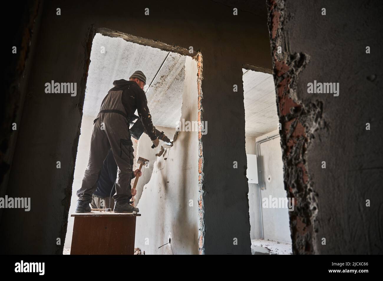 Full length of male builders using hammer drill and sledgehammer while ...