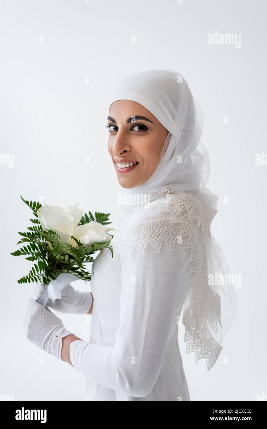 cheerful muslim bride in gloves and wedding dress holding calla lily ...