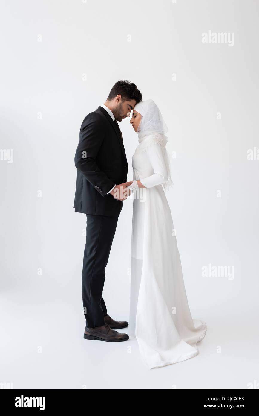 side view of muslim married couple holding hands and standing on grey Stock Photo - Alamy