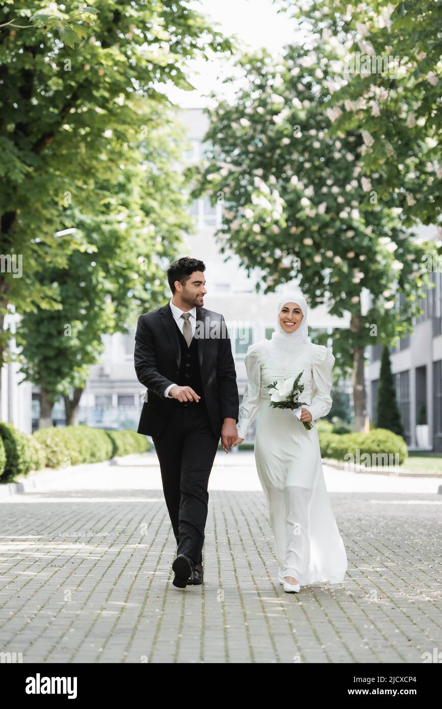 happy groom holding hands with muslim bride with wedding bouquet and ...