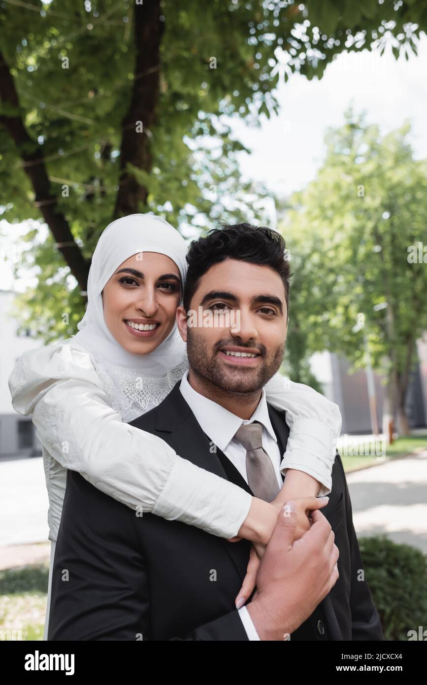 pleased bride in hijab hugging cheerful muslim groom in suit Stock ...