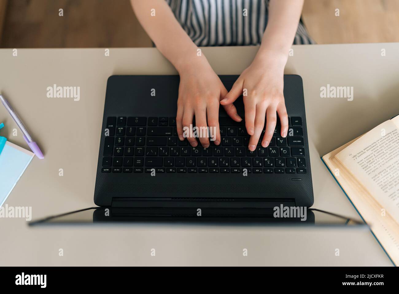 Close-up top view of unrecognizable child school girl typing on laptop ...
