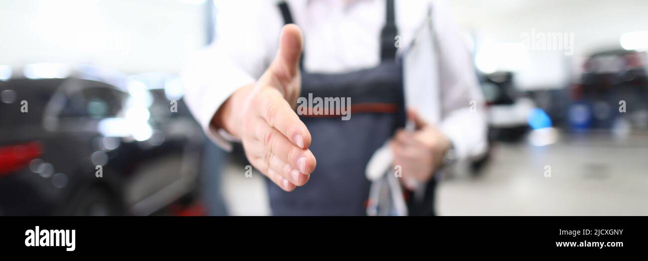 Male repairman stretching out his hand for handshake in car repair shop ...