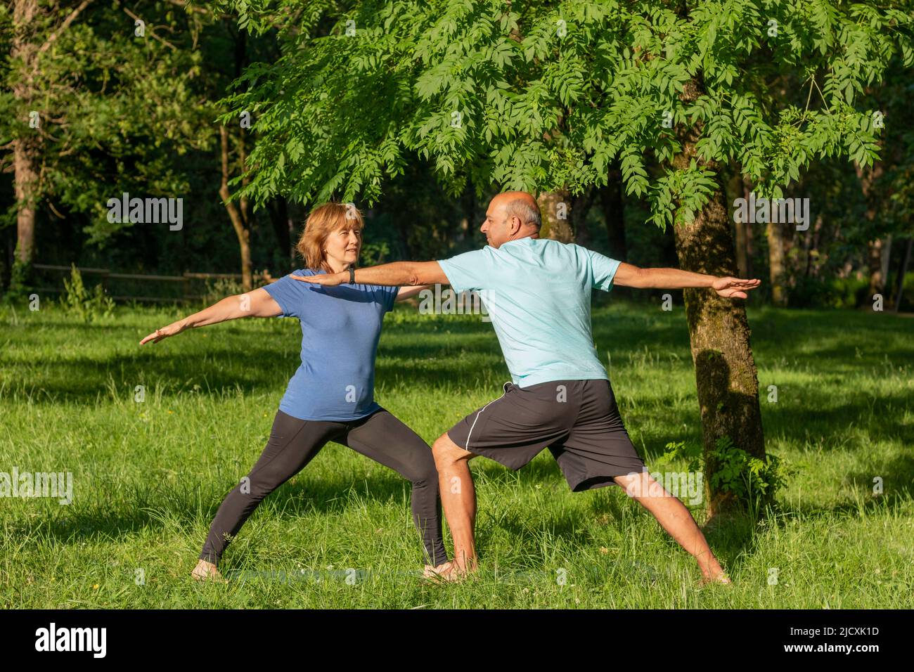 Mature couple practising yoga position sideways with arms open standing ...