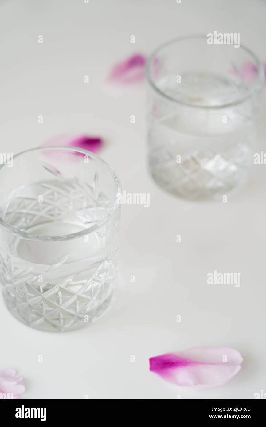 close up view of glasses with fresh water near floral petals on white ...