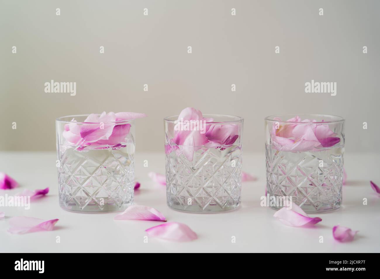 crystal glasses with floral petals and tonic on white tabletop isolated ...