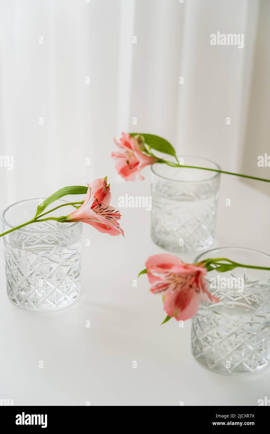 crystal glasses with water near alstroemeria flowers on white tabletop ...