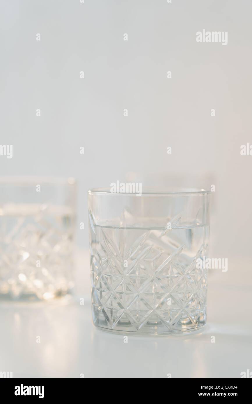 glass with faceted pattern and pure water on grey blurred background ...